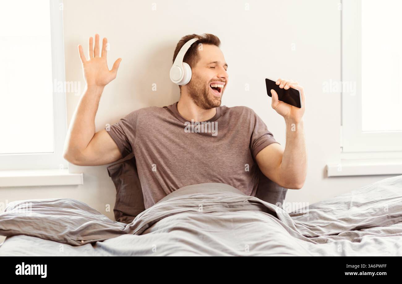 Man Wearing Headphones Singing Song Sitting In Bed At Home Stock Photo ...