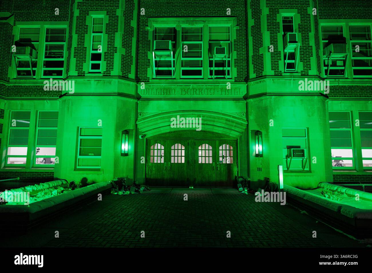Berkey Hall is illuminated in green as community members leave flowers ...
