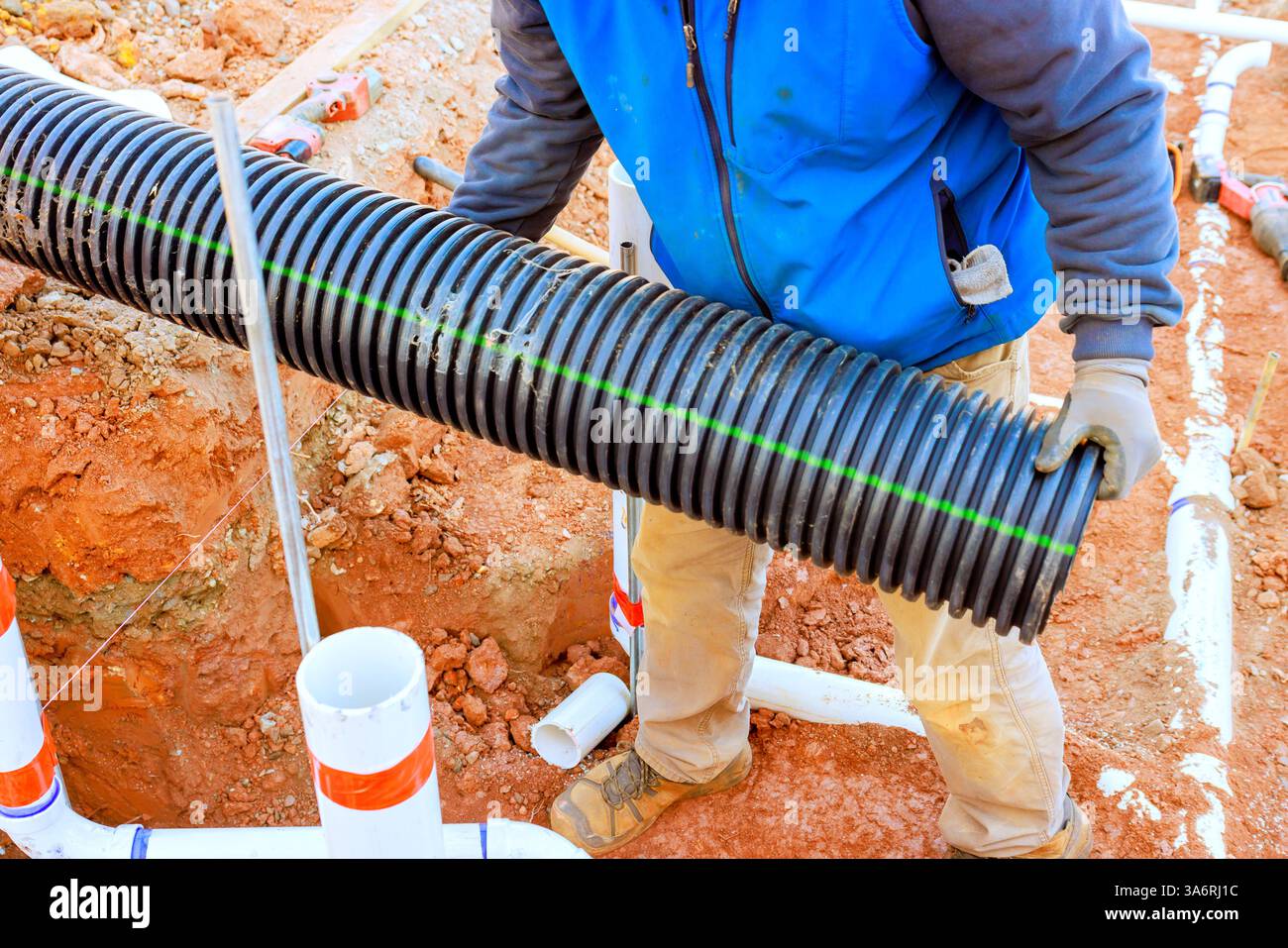 Laborer handles black drainage pipe while working on construction area ...