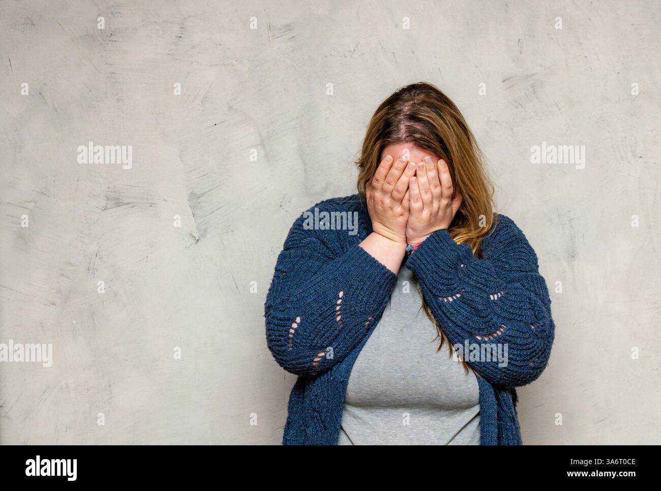 A beautiful mother stands alone against a plain background, hiding her ...