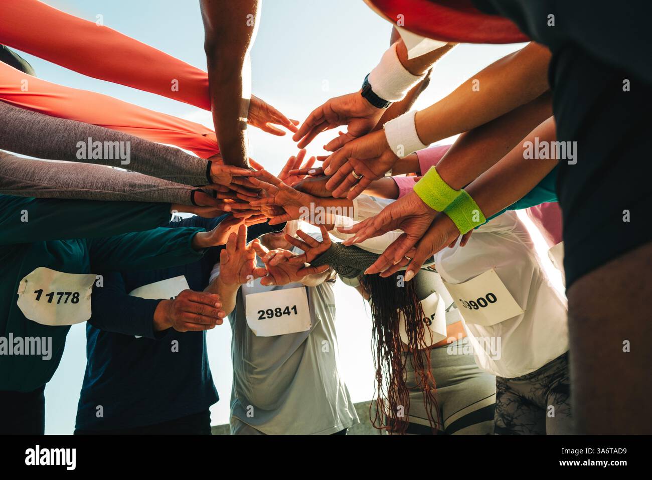 A group of runners gathers in a team spirit huddle, placing their hands ...