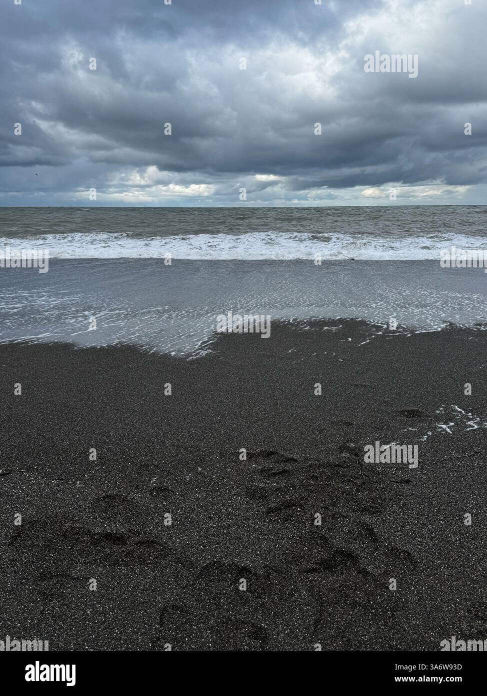Ocean waves washing over a black sand beach under a moody, overcast sky ...