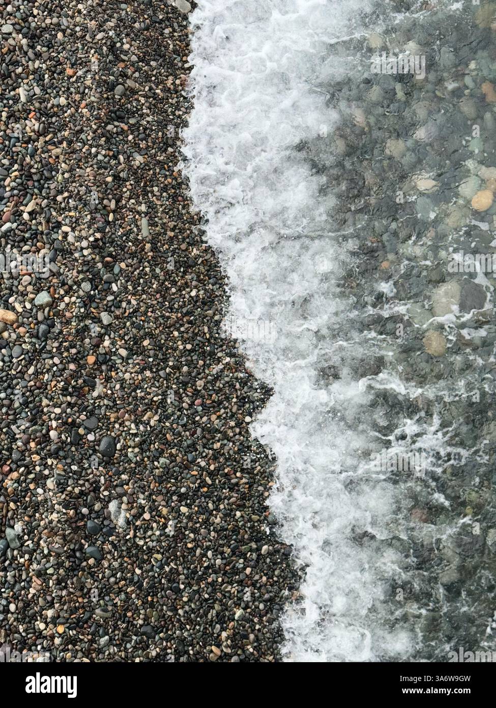 Aerial view of gentle ocean waves washing over a pebble beach, showing ...