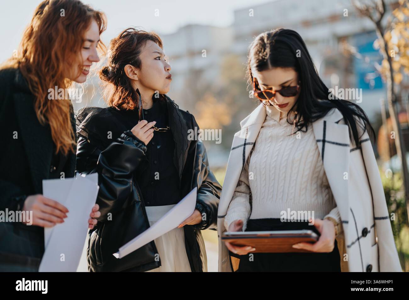 Three young women engaging in outdoor discussion with documents and a ...