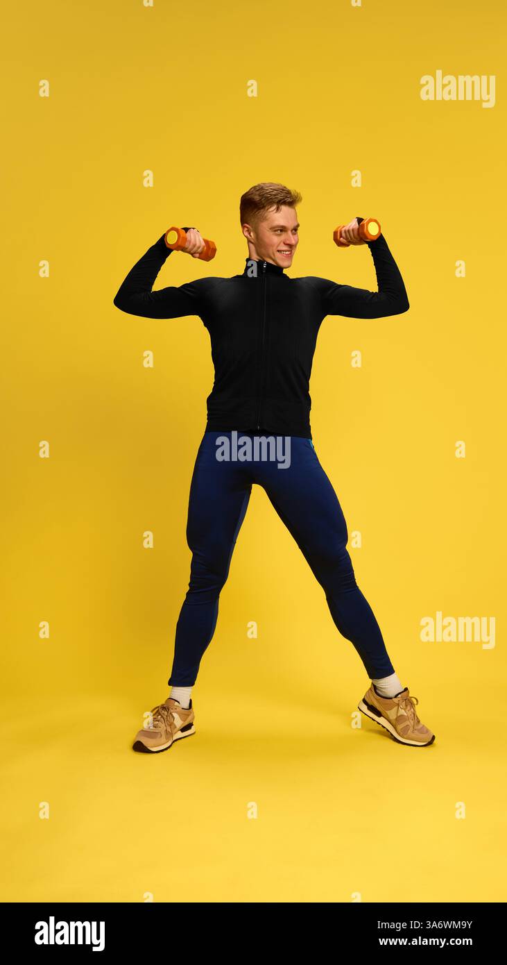 Fit man lifting dumbbells in biceps curl pose against yellow background ...