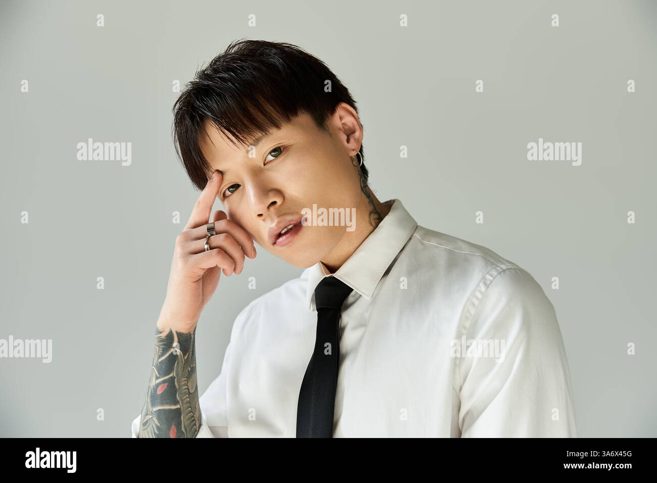 A stylish young man showcases his tattoos, deep in thought in a modern ...
