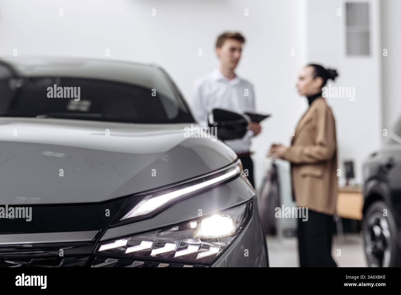 A car sales manager shows a vehicle to a customer in a luxurious ...