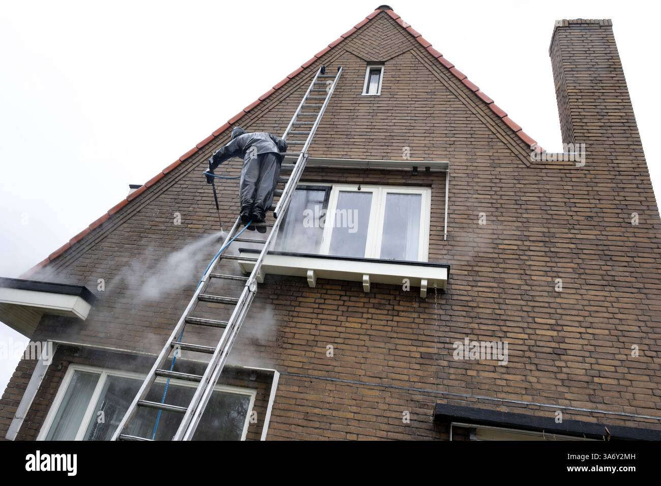 Man in waterproof suit cleans dirty brick facade of residential house ...