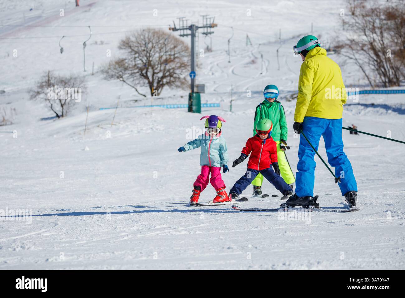 On a ski slope, coach giving instructions and group of children having ...