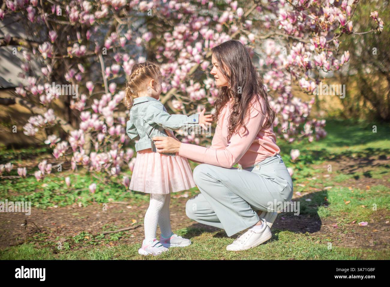 Trendy mom with her little daughter under blooming magnolia trees in a ...