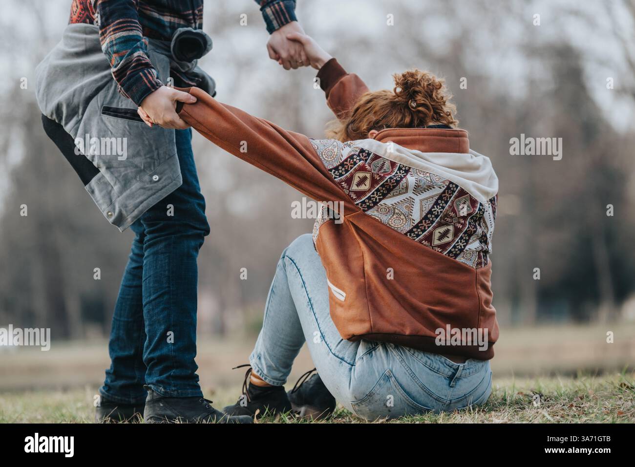 Person assisting another individual to stand in an outdoor park setting ...