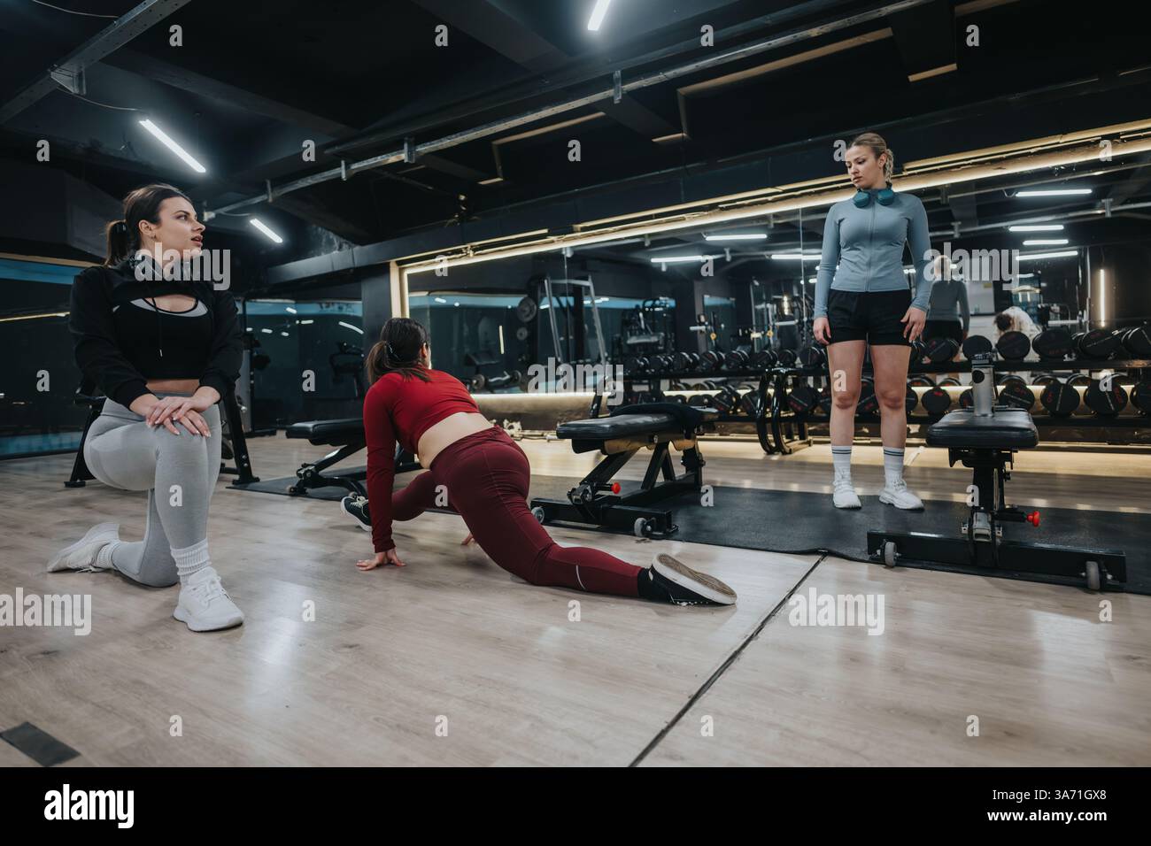 Three women exercising together in a modern gym with stretching and ...