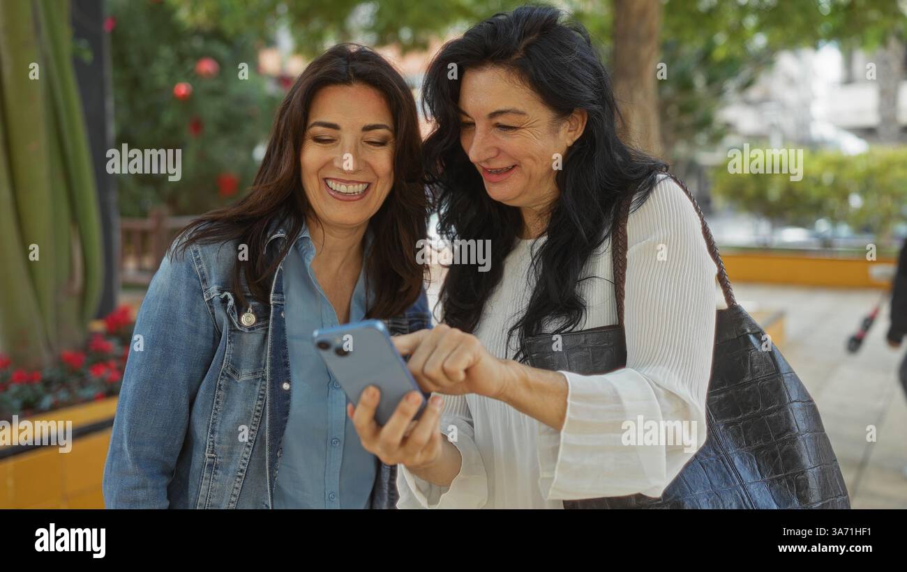 Women laughing together while looking at a phone outdoors in a city ...