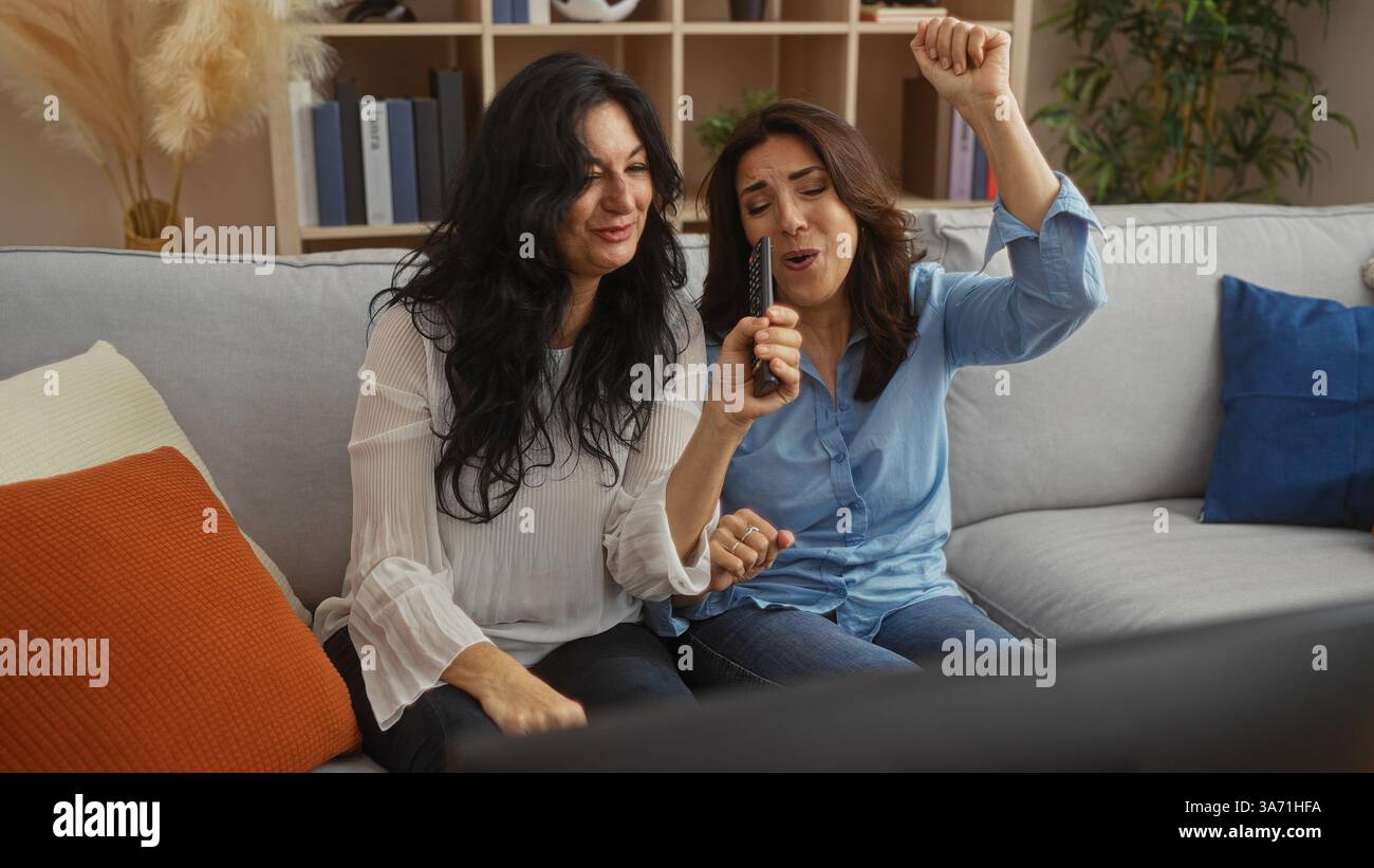 Two women joyfully singing and dancing in a living room using a remote ...