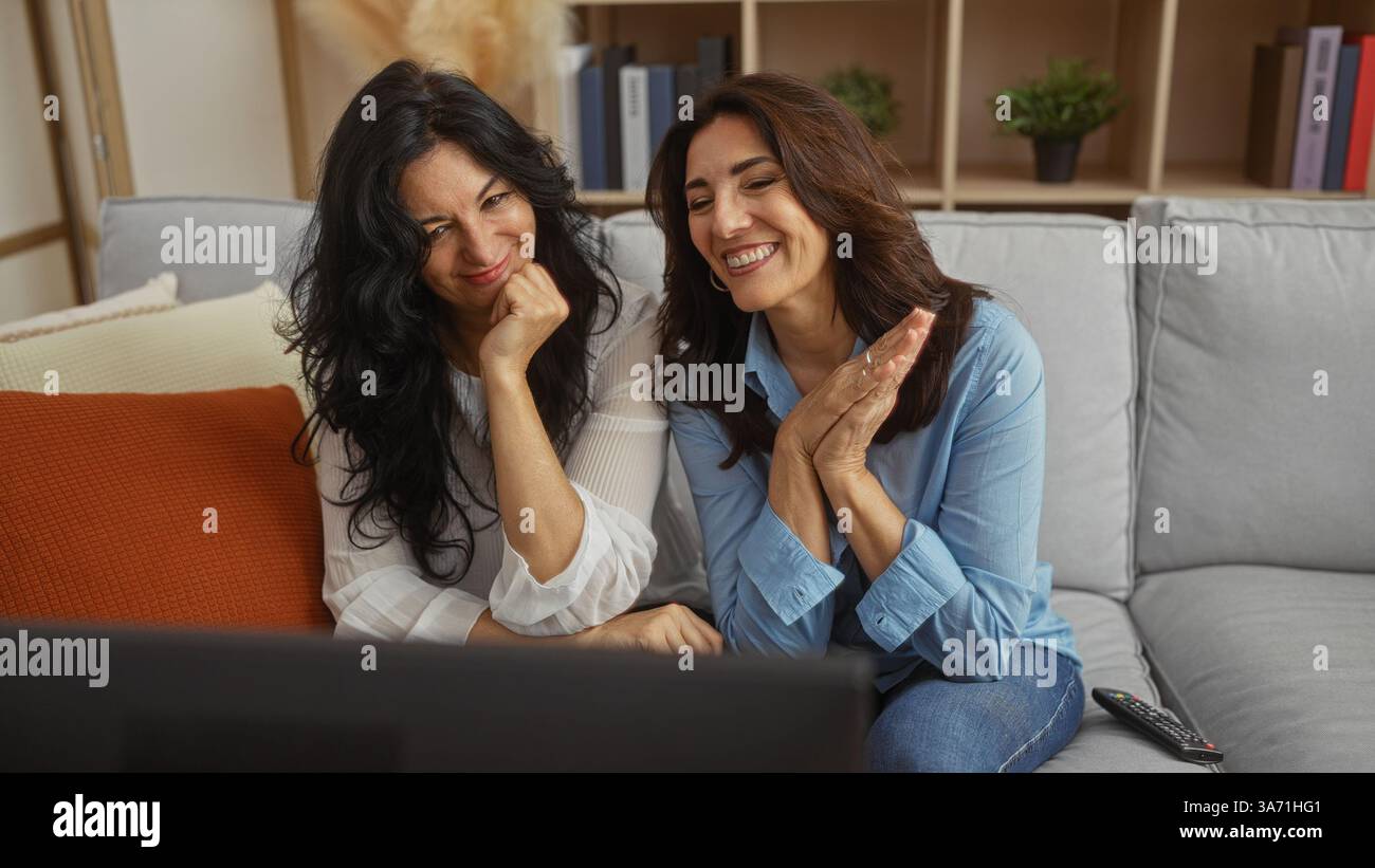 Middle-aged women laughing together in a cozy living room, symbolizing familial love and ...