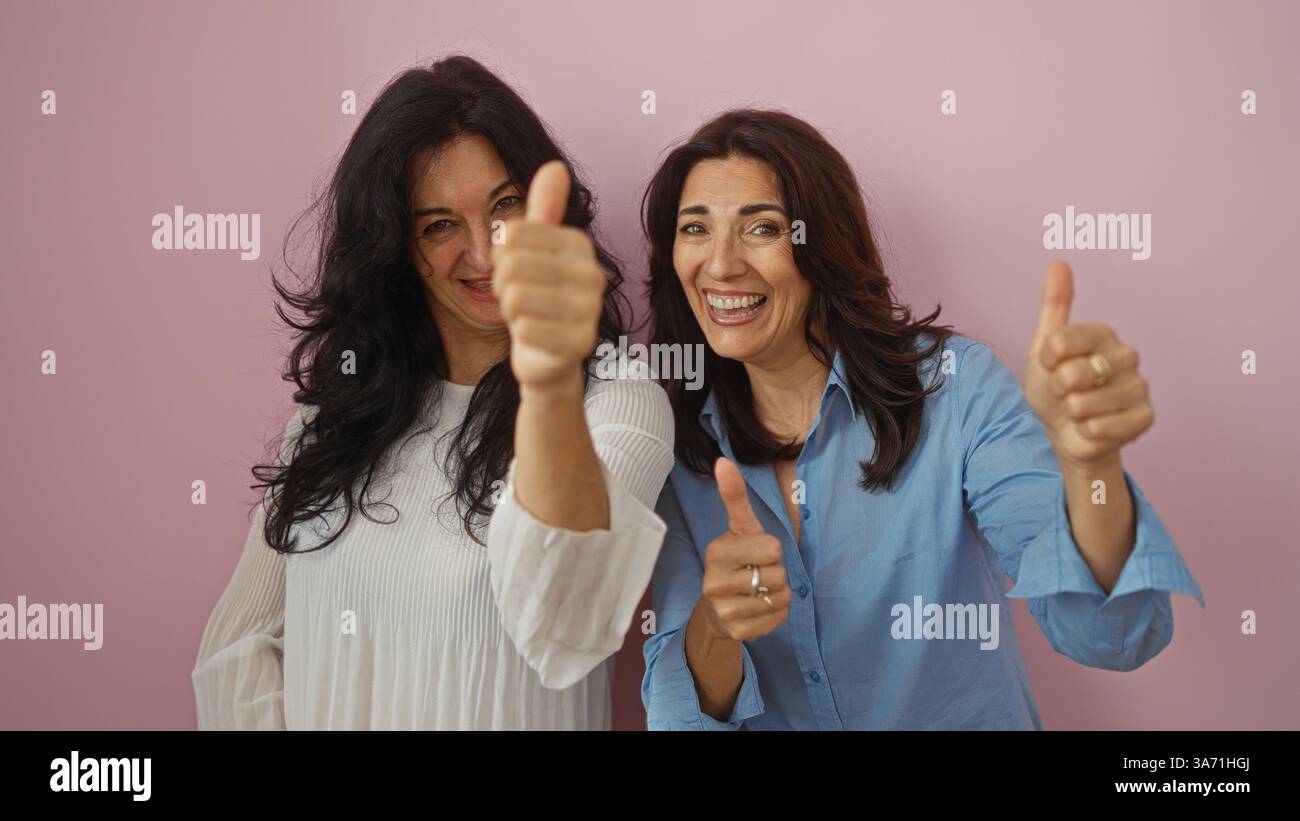 Two middle-aged women smiling happily together against a pink wall ...
