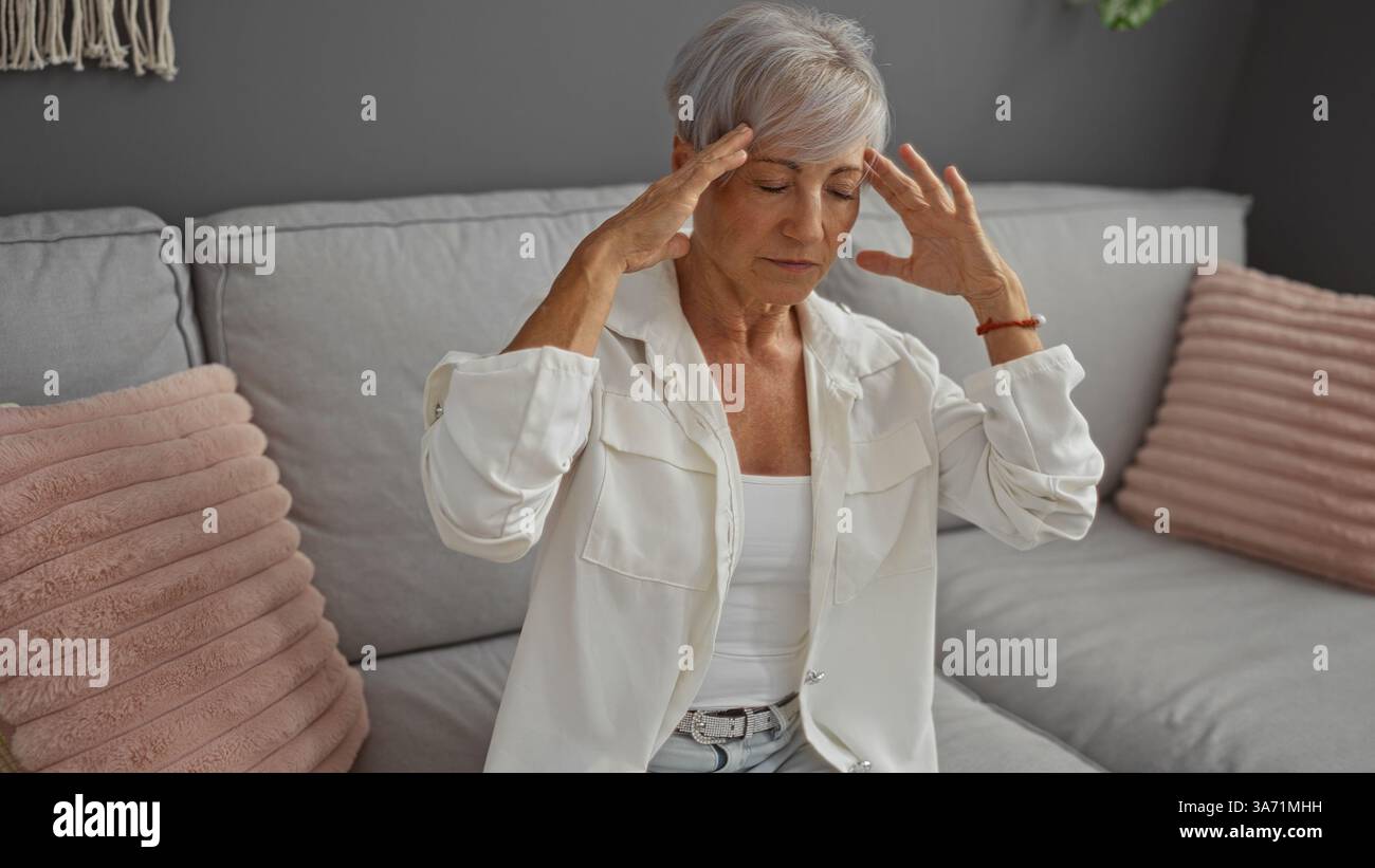 Mature woman with short grey hair seated in a living room experiencing ...