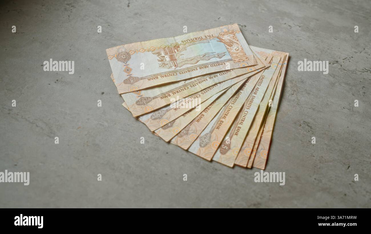 Five dirham uae banknotes scattered on a concrete surface, highlighting ...