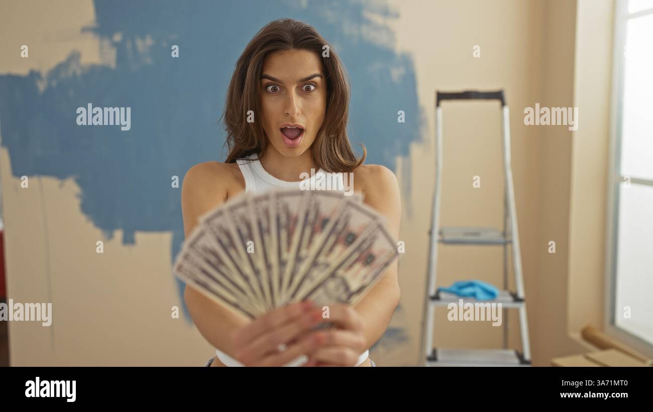 Woman holding money with surprised expression in home interior while ...