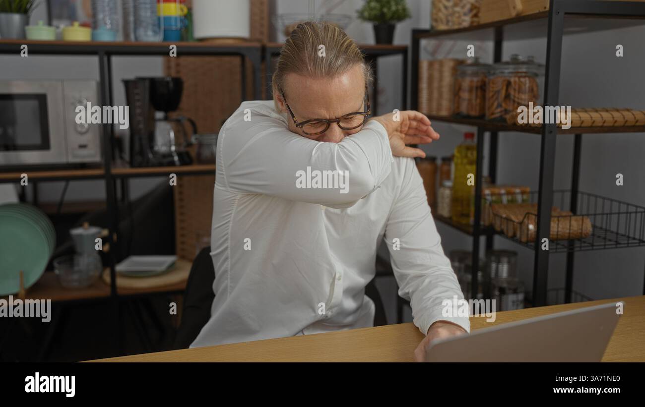 Blonde mature man sneezing in office interior with shelves and laptop ...