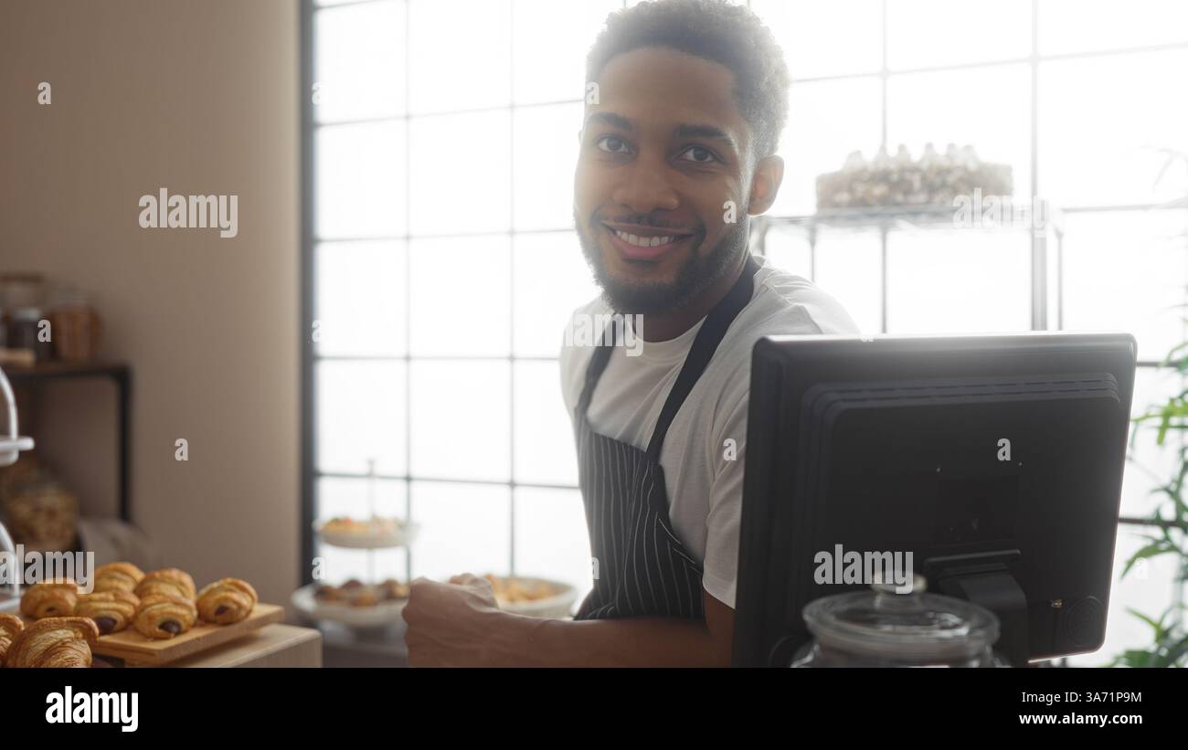 Young man smiling behind counter in bakery cafe with pastries displayed ...