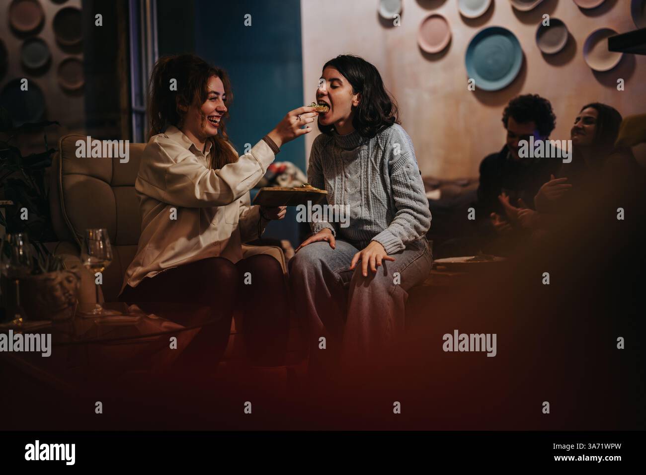 Two friends sharing food together in a stylish lounge setting Stock ...