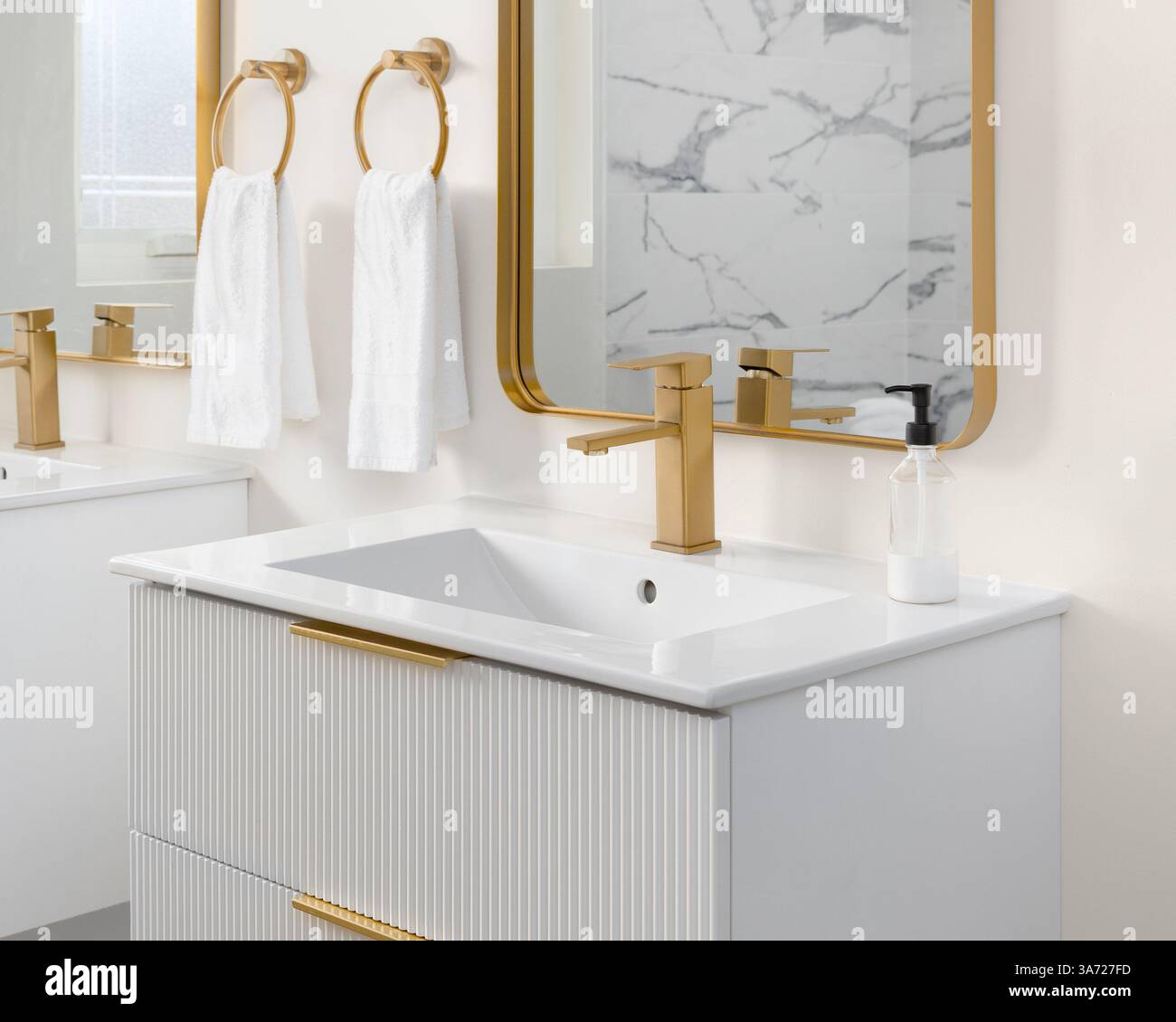 A bathroom detail with a white fluted floating cabinet, gold faucet on ...