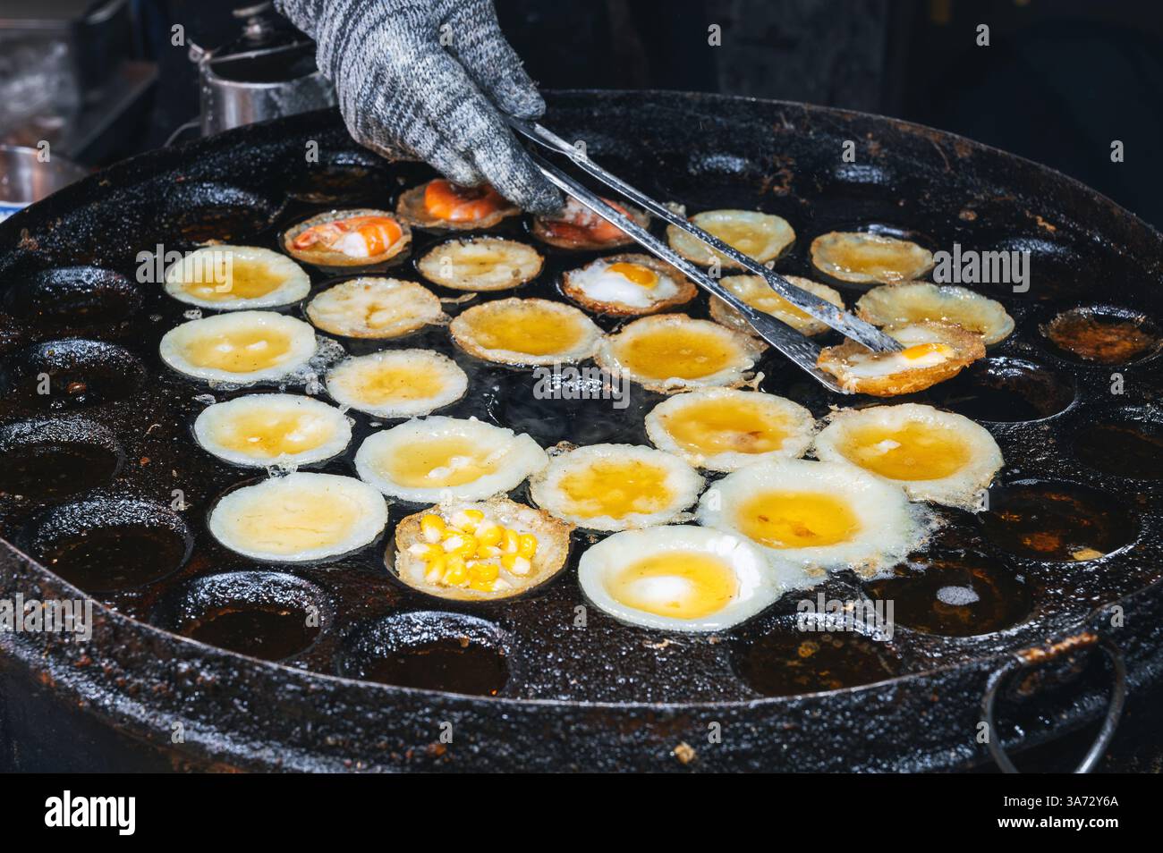 cooking a traditional Vietnamese dish Banh Khot with shrimps and corn ...