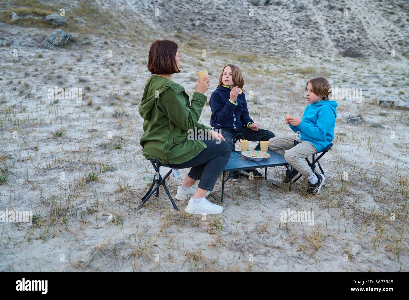 Family enjoying an outdoor picnic in a sandy field, sitting on small ...