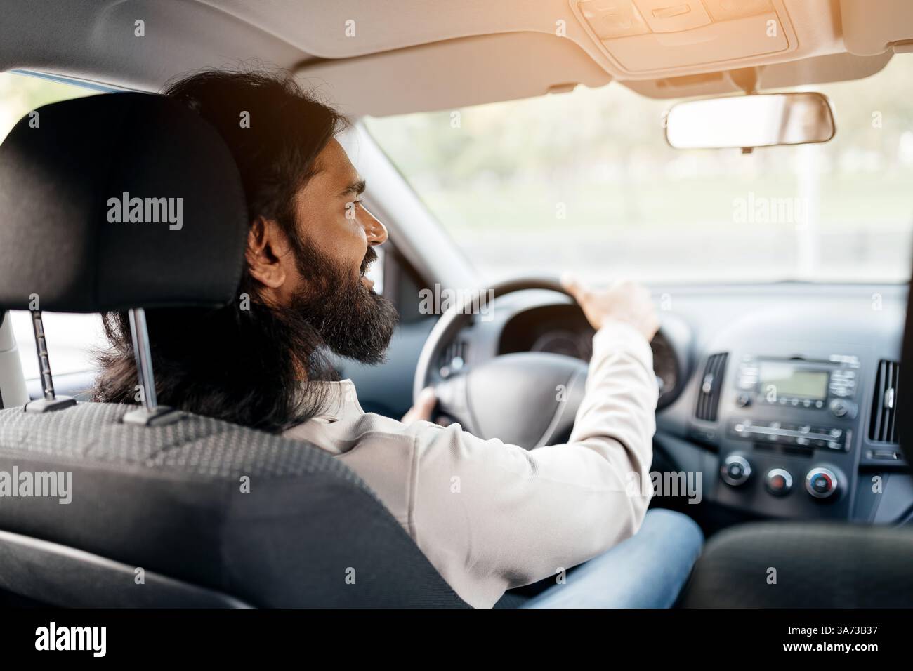 Rear view of Indian man driving car, looking forward and holding wheel ...