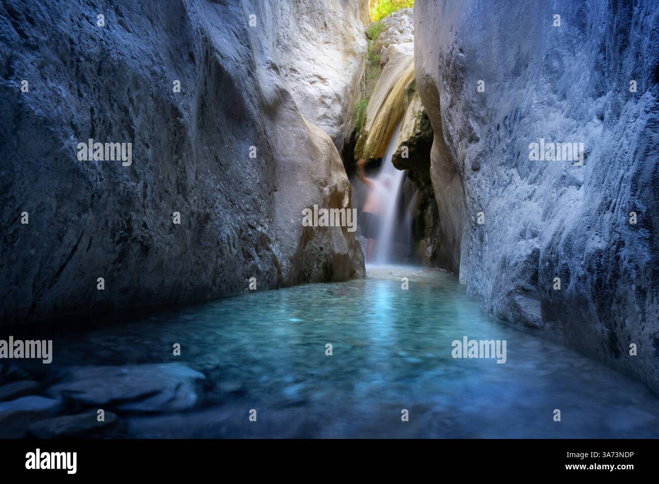 An anonymous man bathes in a small waterfall in the cannon of a small ...