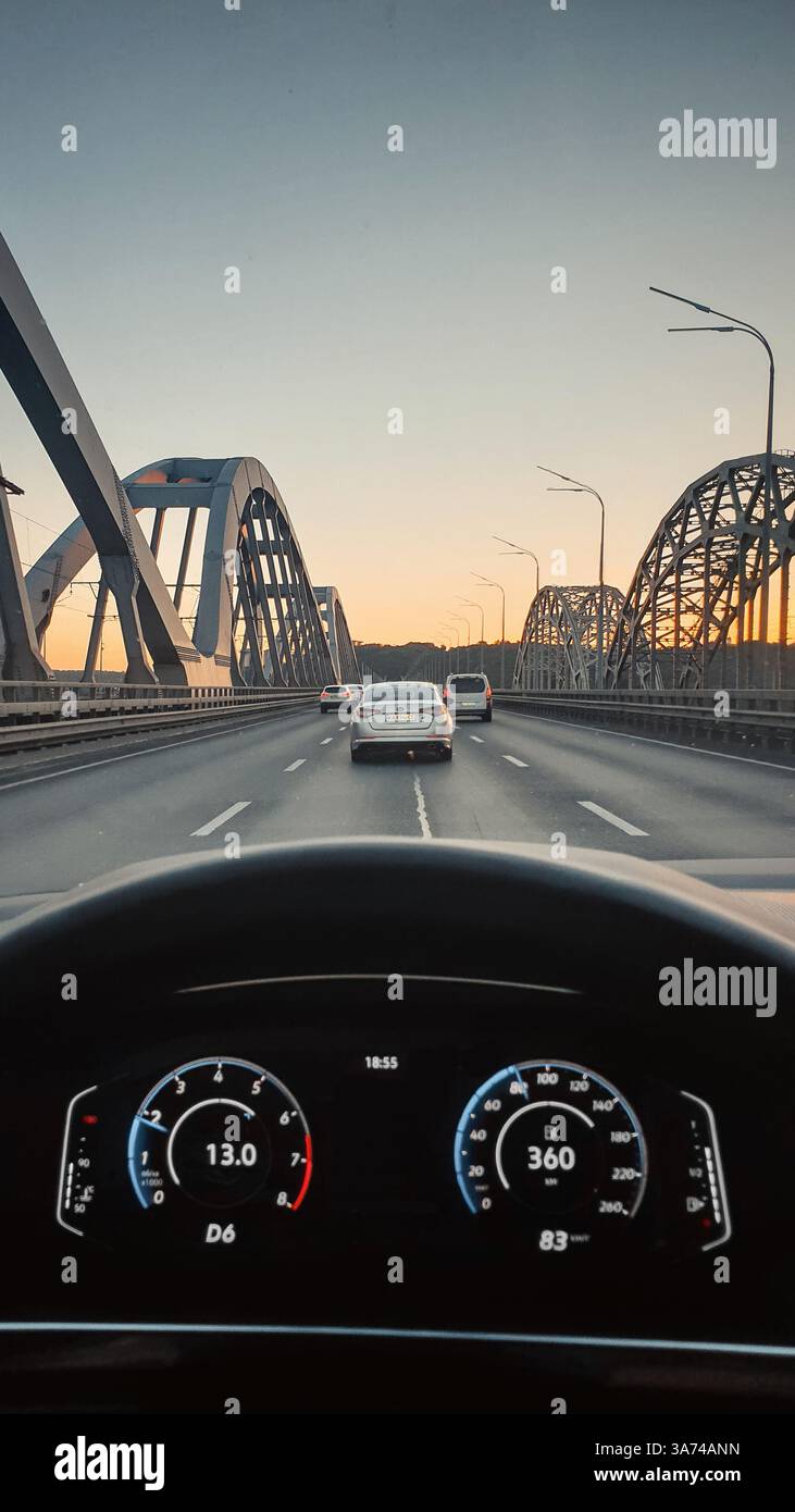 First person view of driving a car over a bridge at sunset. Driver's ...