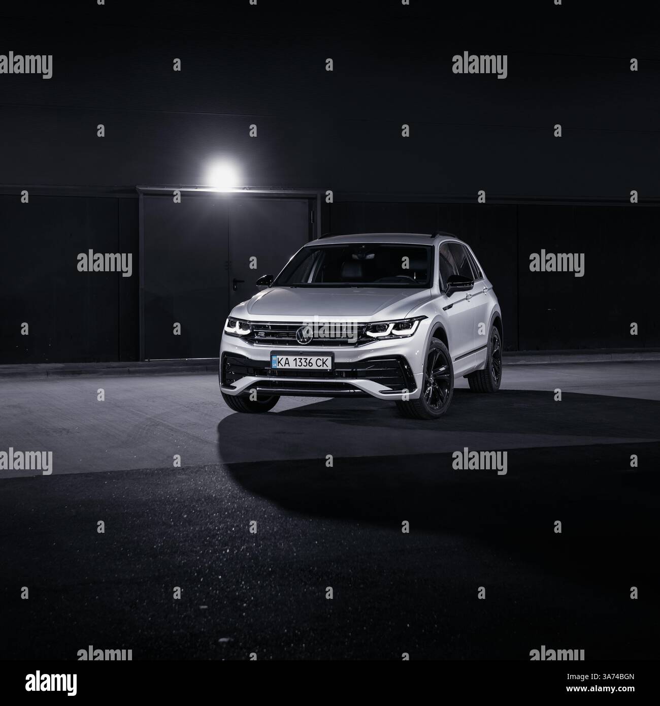 Silver Volkswagen Tiguan R-line near warehouse at night. Front view of ...