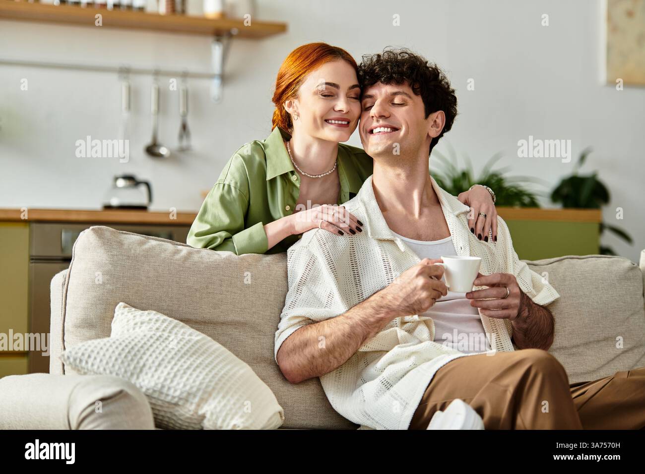 A young couple shares laughter and warmth in their cozy living space, sipping tea and bonding ...