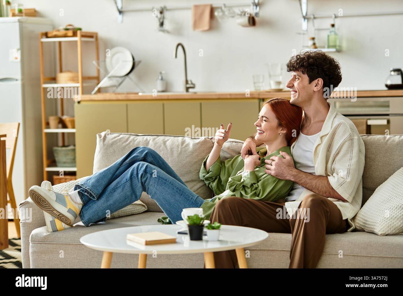 A young couple smiles and laughs together while lounging on their couch ...