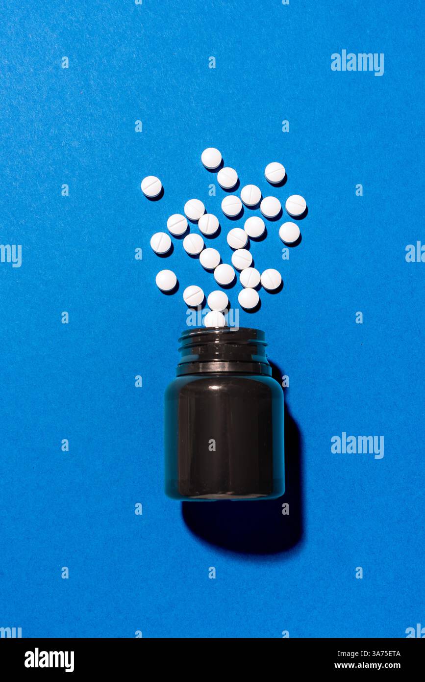 Melatonin tablets spill from blank container on dark blue background ...