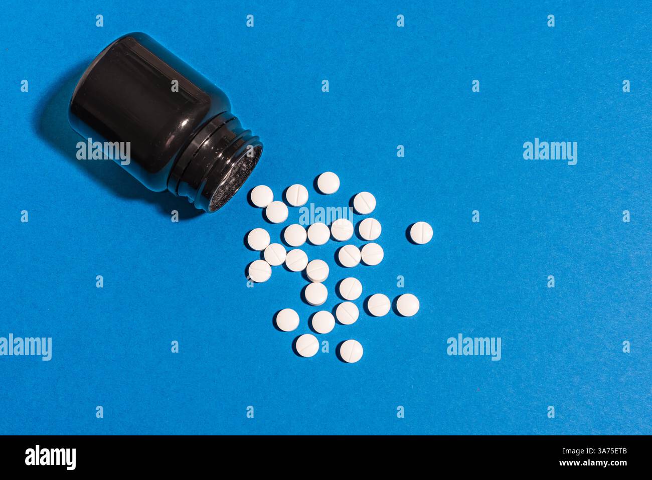 Melatonin tablets spill from black container on dark blue background ...
