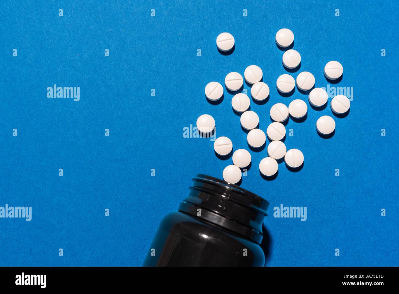 Melatonin tablets spill from black container on dark blue background ...