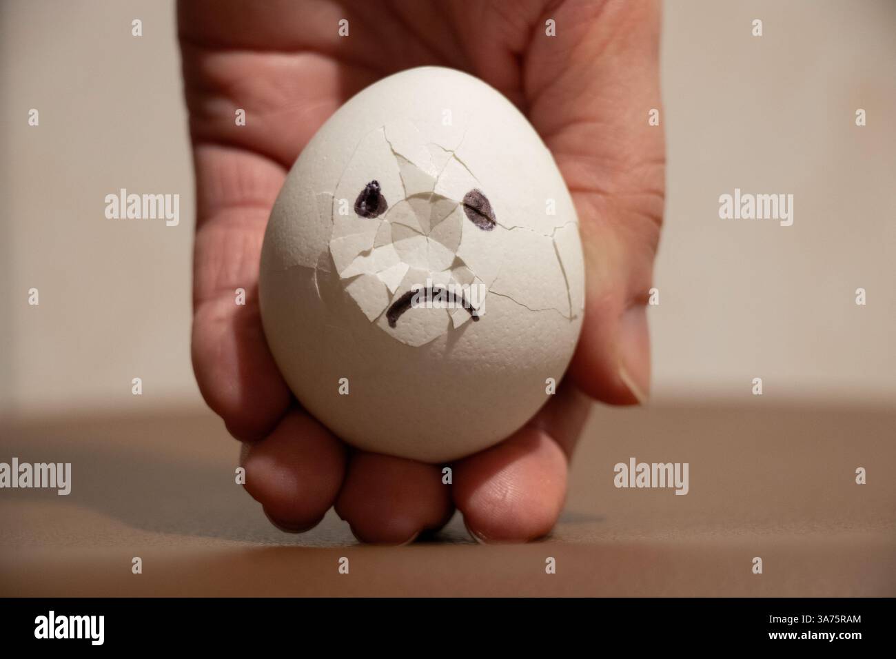 Woman holding cracked chicken egg with sad and sorrowful emotions drawn on the egg, egg shortage ...