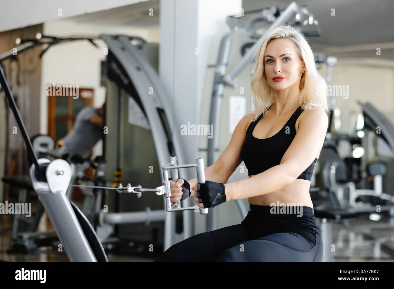Strong female athlete exercising back muscles using cable row machine ...