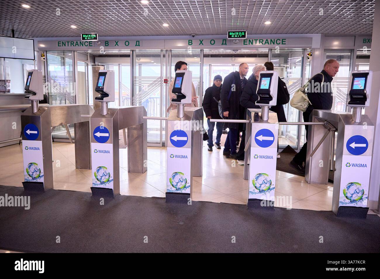 A modern entrance, people pass through automated turnstiles to the ...