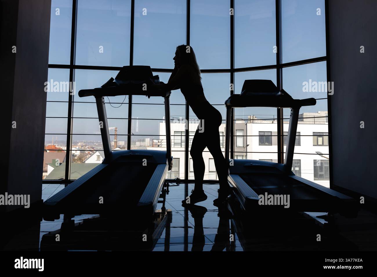 Silhouette of an athletic woman resting against a treadmill in a gym ...