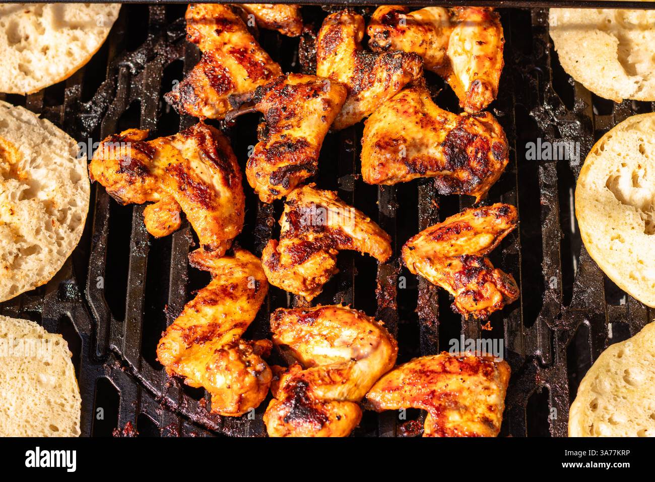 Golden chicken wings with perfect char marks grilling alongside buns on ...