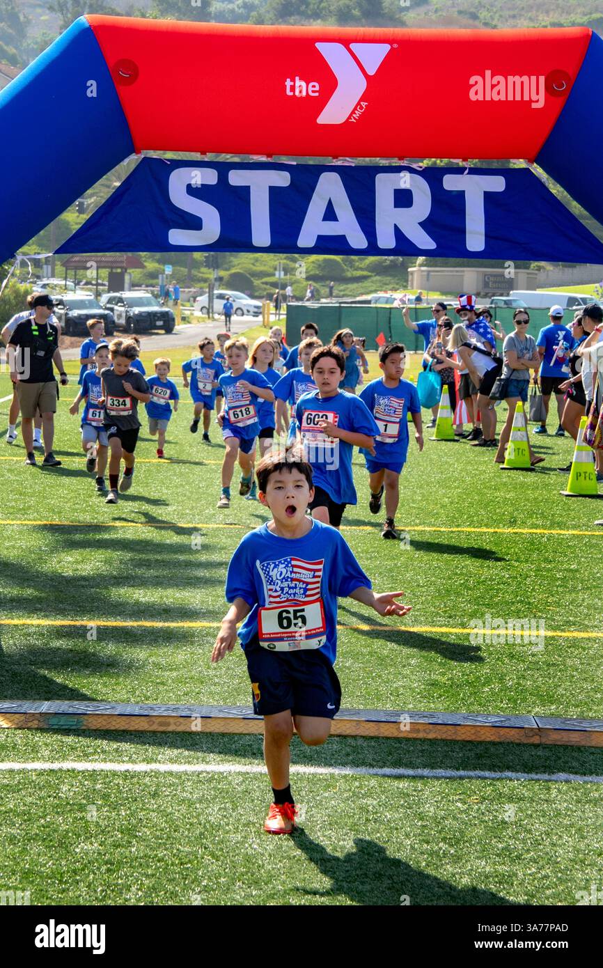 A Caucasian boy crosses the finish line of a foot race at a Fourth of ...