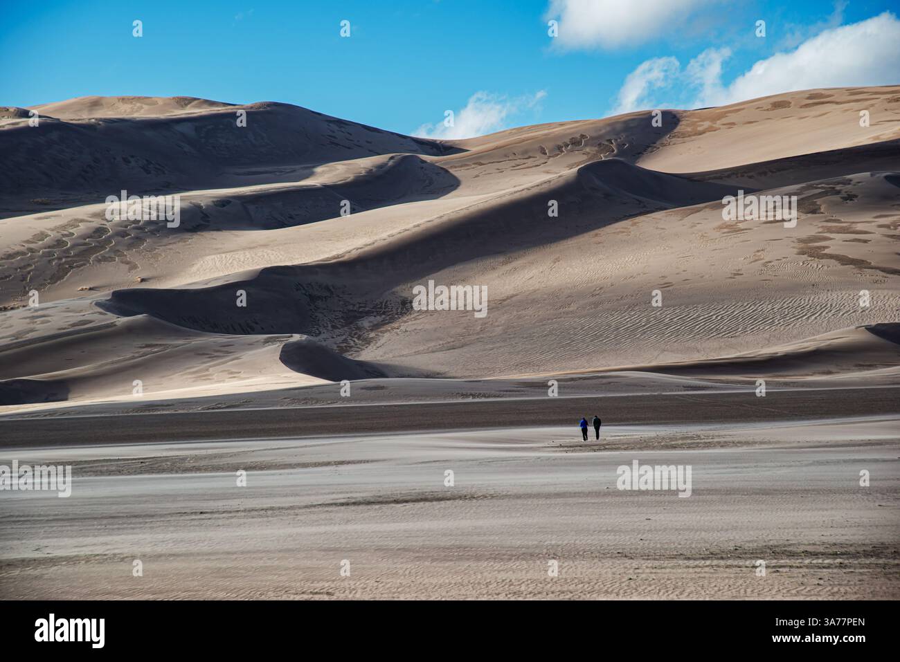 Two people walk toward the sand dunes in late afternoon light. Great ...