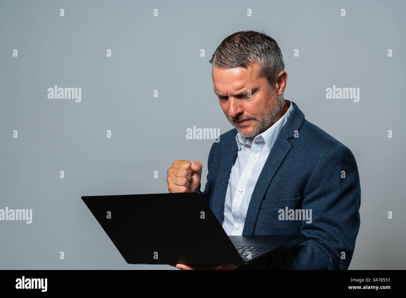Middle aged man in classic business suit stares intently screen with his hand clenched into fist ...