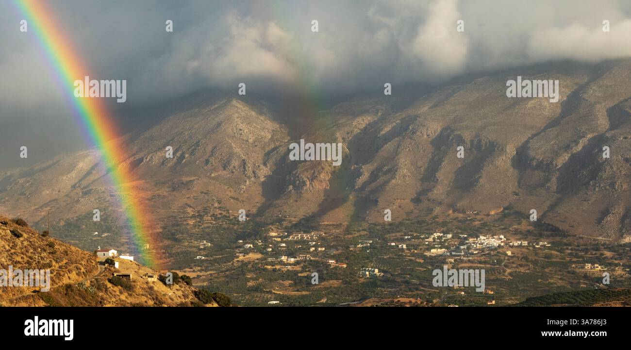 A vibrant rainbow arcs across a mountainous landscape, touching down ...