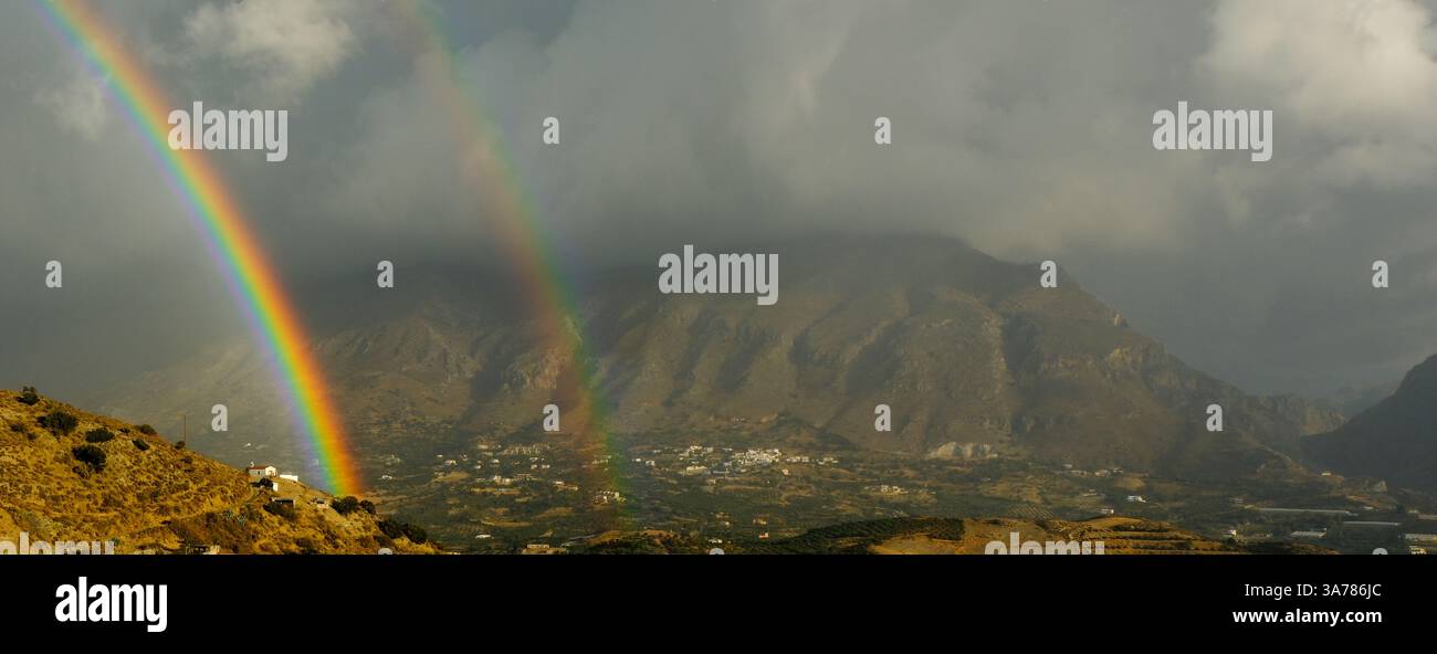 After a rain shower, a vibrant double rainbow arches over a mountainous ...