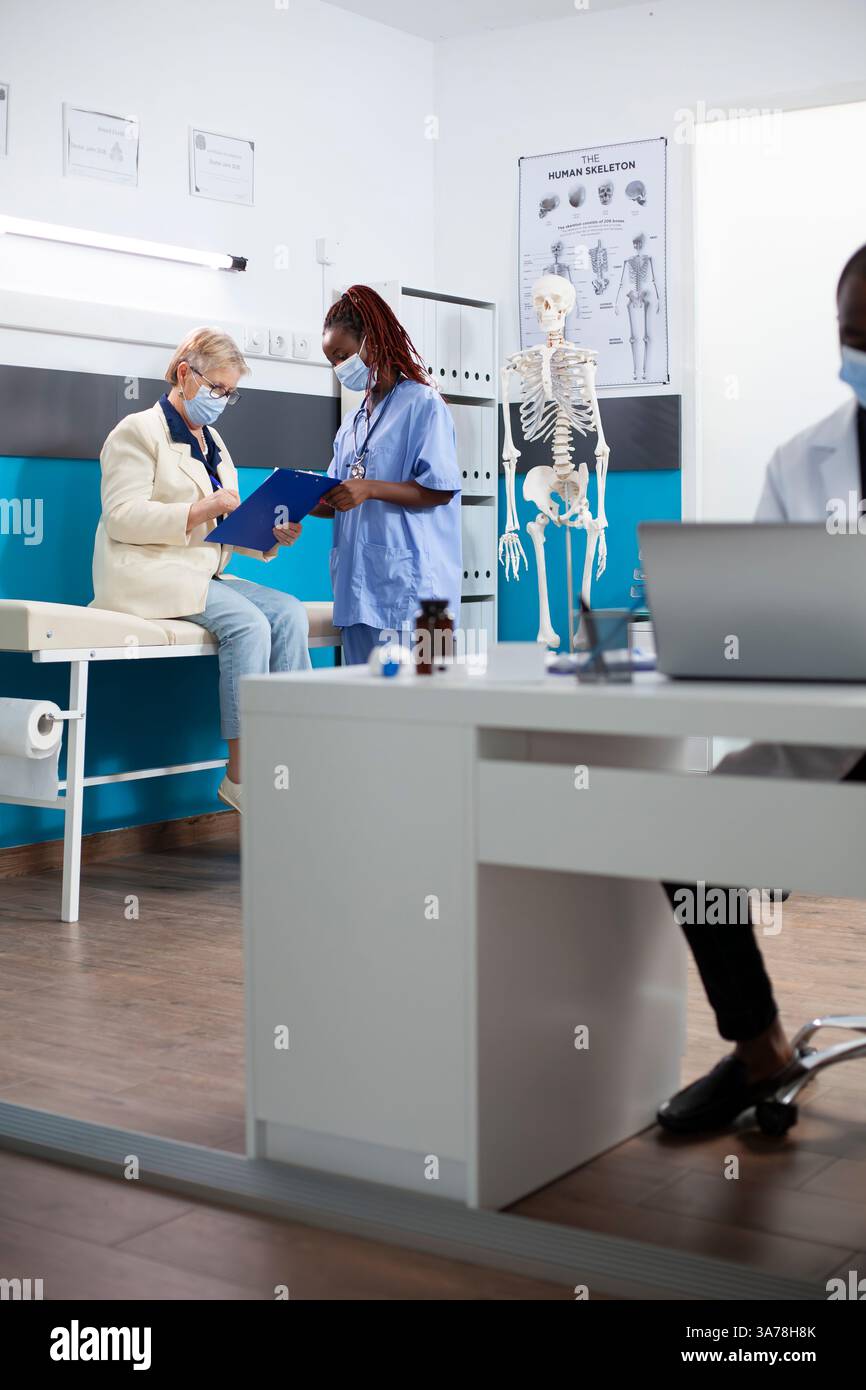 Caucasian senior woman sits in hospital room writing on clipboard as ...