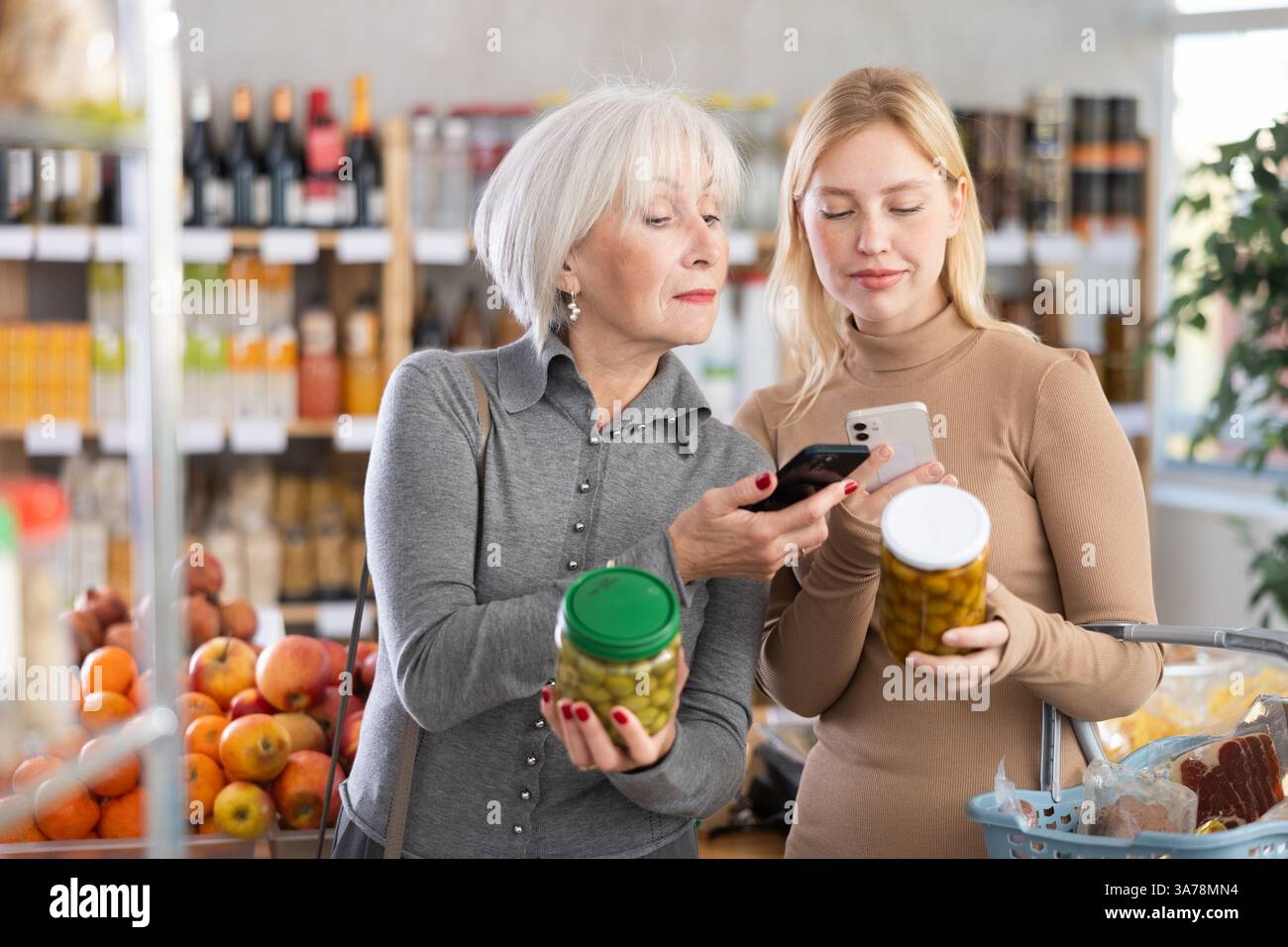 Elderly mother and her adult daughter scan QR code on jar canned green ...